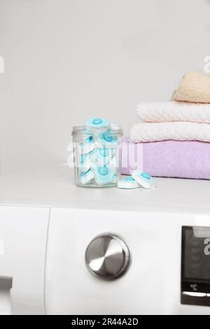 Jar with water softener tablets on laundry basket near washing machine ...