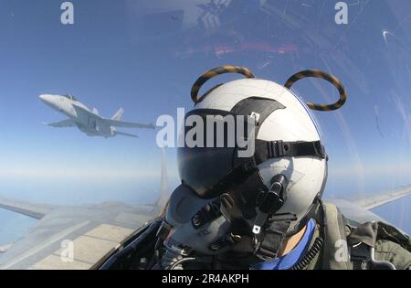 A Fighter Squadron 143 (VF-143) F-14B Tomcat aircraft flies over the desert as an oil well burns ...