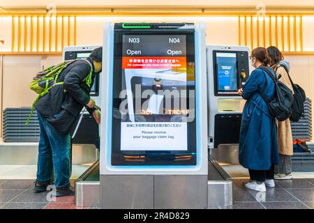 Check-in baggage machine with 2 women checking-in using the luggage tag ...