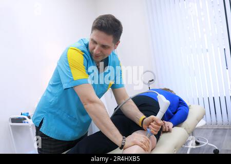 Osteopath treating knee to patient with shock wave therapy in clinic ...