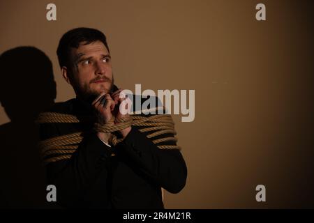 Scared man tied up and taken hostage on dark background. Space for text ...
