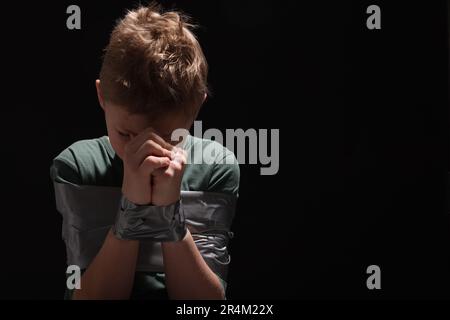 Little boy tied up and taken hostage on dark background. Space for text ...