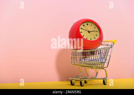 A supermarket trolley with old vintage alarm clock on pink and yellow ...