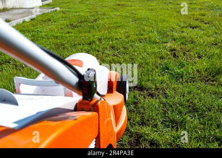 A small motorized electric mower standing on the lawn, it is orange in ...