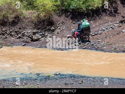 A local man on heavily loaded motorbike trying to cross a river. Kenya ...