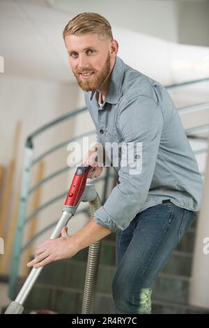 Handsome man cleaning office with vacuum cleaner Stock Photo - Alamy