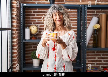 Middle age woman artist drinking coffee standing at art studio Stock ...