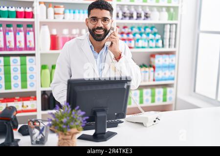 Young arab man pharmacist talking on telephone using computer at ...