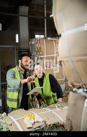 Young sorter in vest and protective gloves putting cardboard in sack ...