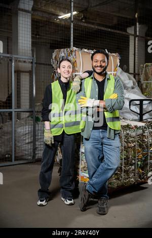 Young sorter in vest and protective gloves putting cardboard in sack ...