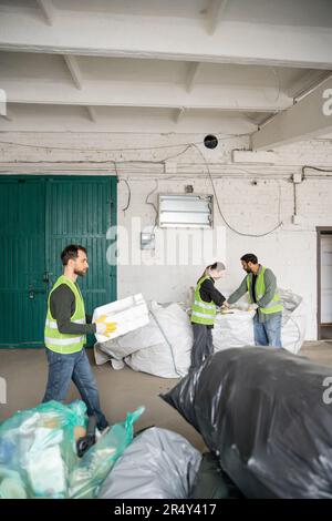 Interracial workers in high visibility vests and gloves soring trash in ...