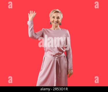 Stylish mature woman waving hand on red background Stock Photo - Alamy