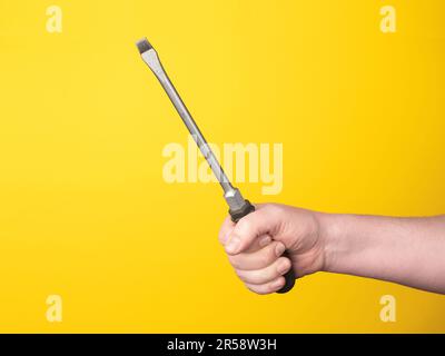 A male hand is holding a very large screwdriver. Yellow background, no ...