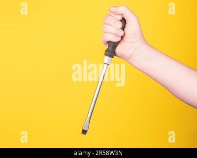 A male hand is holding a very large screwdriver. Yellow background, no ...