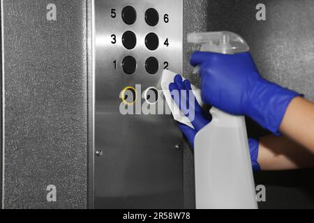 Woman wiping buttons of elevator`s panel with detergent and paper ...