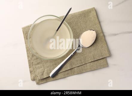Glass bowl of agar-agar jelly and spoon with powder on white marble ...
