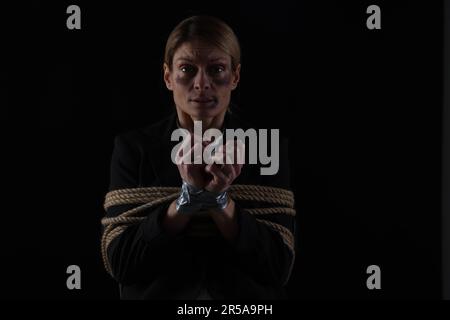 Scared woman tied up and taken hostage on dark background. Space for ...