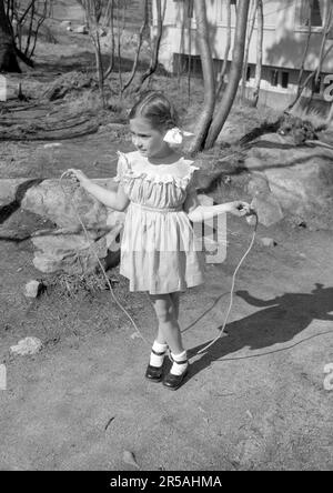 In the 1950s. A girl in a nice dress is jumping rope, skipping rope ...