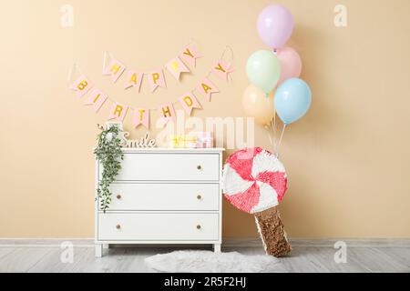 Chest of drawers, pinata, balloons and garland near beige wall in ...