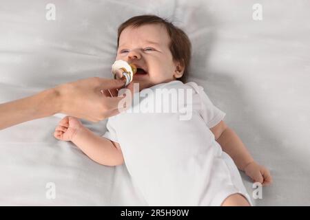 Mother giving pacifier to crying little baby on bed, closeup Stock ...