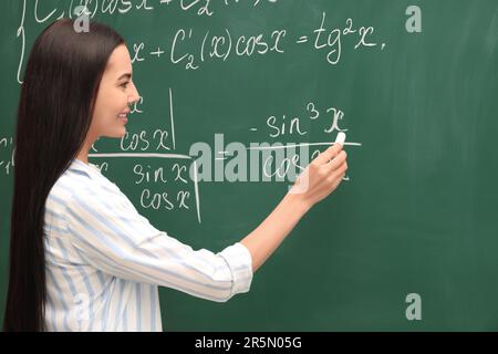 Happy teacher explaining mathematics at chalkboard in classroom Stock ...