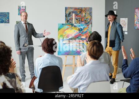 Gallery owner presenting modern art of artist to group of people during ...