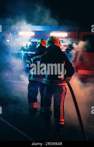Firefighters in protective gear are responding to a building fire, with ...