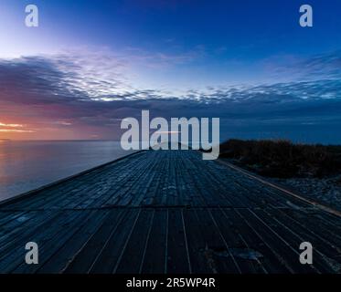 A wooden dock jutting out into a tranquil blue body of water, with a ...