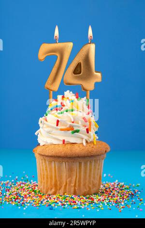 Number 74 blue celebration candle and gold confetti on dark wooden ...