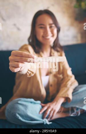 Young Asian woman with pregnancy test sitting on toilet bowl against ...