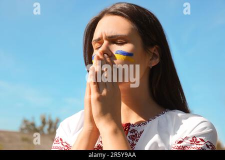 Sad young woman with drawing of Ukrainian flag on face outdoors, space ...