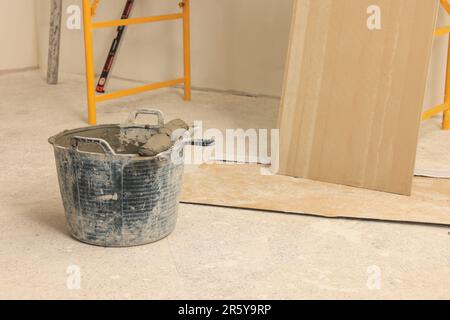 Bucket of adhesive mix and spatula on floor indoors, space for text ...