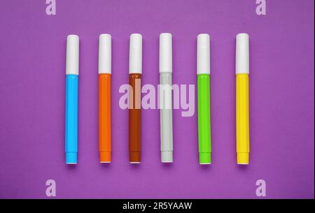 Different colorful markers on purple background, flat lay. Space for ...