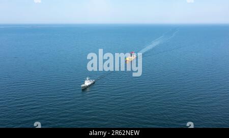 Tug boat travelling across open ocean pulling a yellow barge loaded ...
