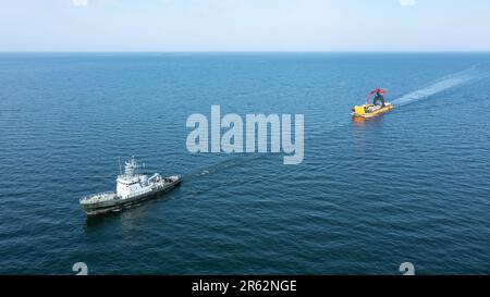 Tug boat travelling across open ocean pulling a yellow barge loaded ...