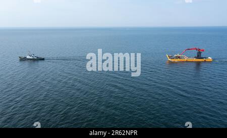 Tug boat travelling across the open ocean pulling a yellow barge loaded ...
