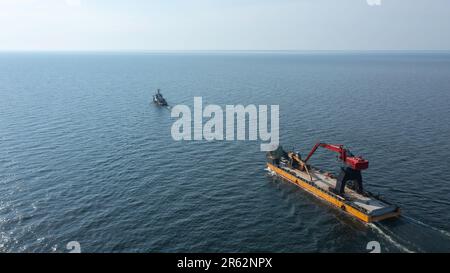 Tug boat travelling across open ocean pulling a yellow barge loaded ...