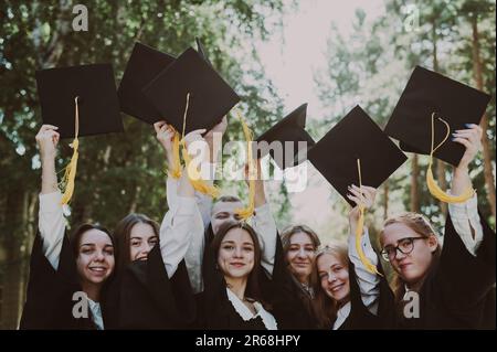 Classmates in graduation gowns throwing hats outdoors Stock Photo - Alamy