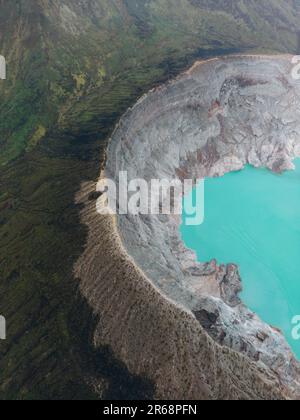 Aerial view of rock cliff at Kawah Ijen volcano with turquoise sulfur water lake at sunrise ...