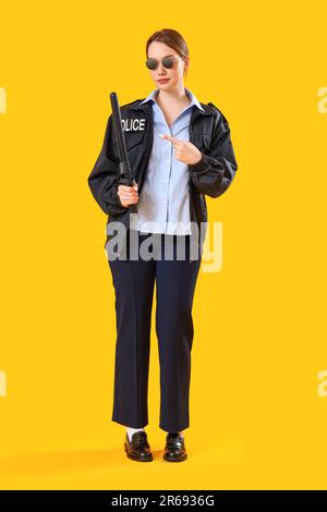 Female police officer with baton on yellow background Stock Photo - Alamy