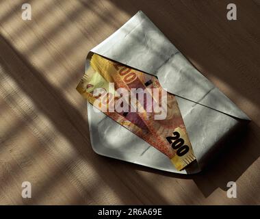 A spreading pile of rand banknotes in an envelope on a wooden surface ...