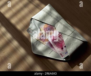 A spreading pile of chinese yuan banknotes in an envelope on a wooden ...