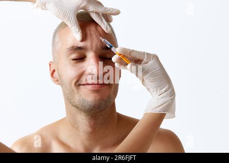 Handsome young man doing cosmetological face injections against white ...