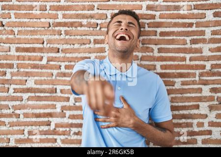 Brazilian young man standing over brick wall doing peace symbol with ...
