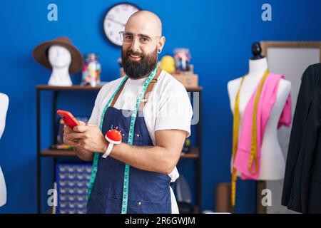 Young bald man tailor smiling confident leaning on clothes rack at ...