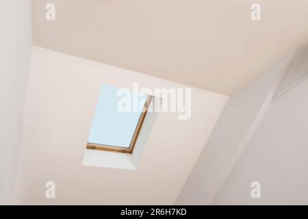Skylight roof window and lamps on slanted ceiling in attic room, low ...