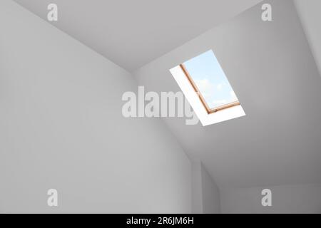 Skylight roof window and lamps on slanted ceiling in attic room, low ...
