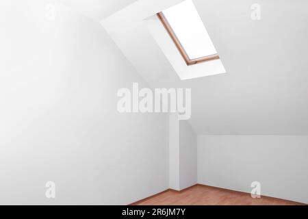 Skylight roof window and lamps on slanted ceiling in attic room, low ...