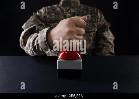 Serviceman pressing red button of nuclear weapon at black table ...