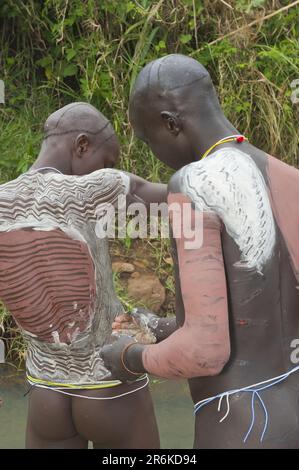 Surma man painting warrior's body, clay and mineral paint, in front of Donga stick fighting ...